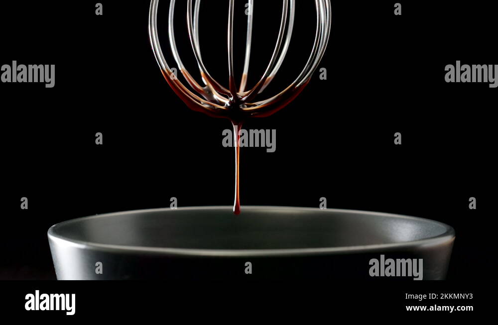 Last drop of liquid chocolate is dripping from steel whisk on black ...