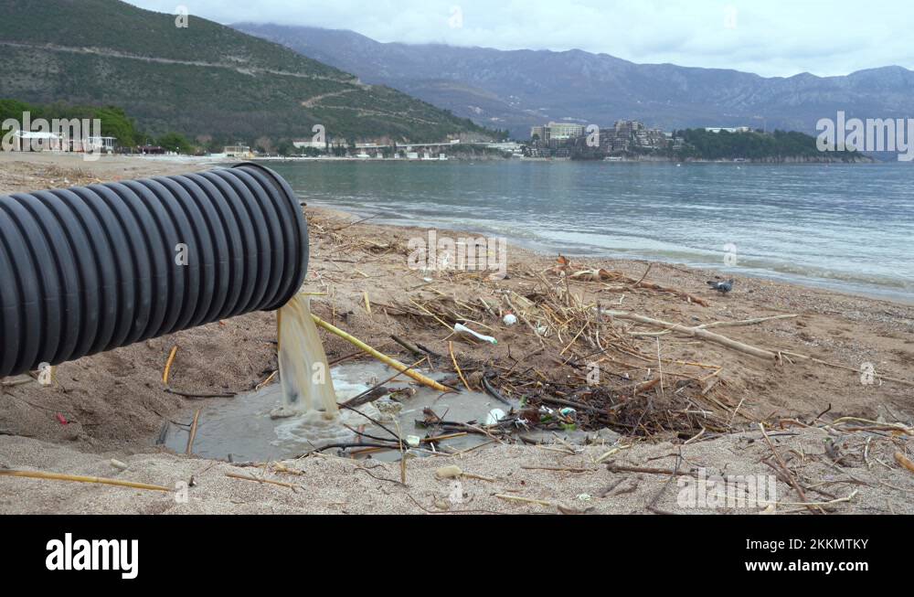Sewage drains from sewer pipe into muddy puddle on littered beach ...