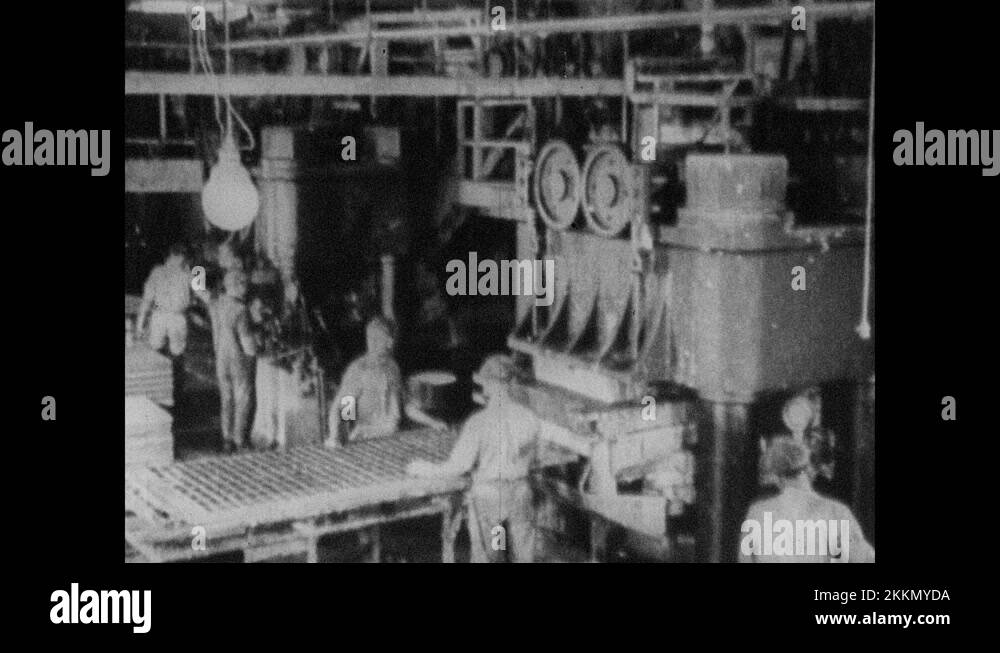 1930s: Corrugated asbestos panels roll off of a factory line. Workers ...