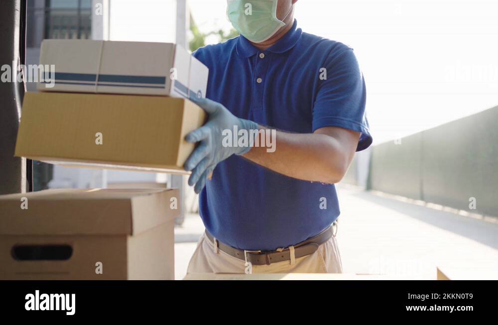 Blue delivery man arranges parcels from the trunk of the car and ...