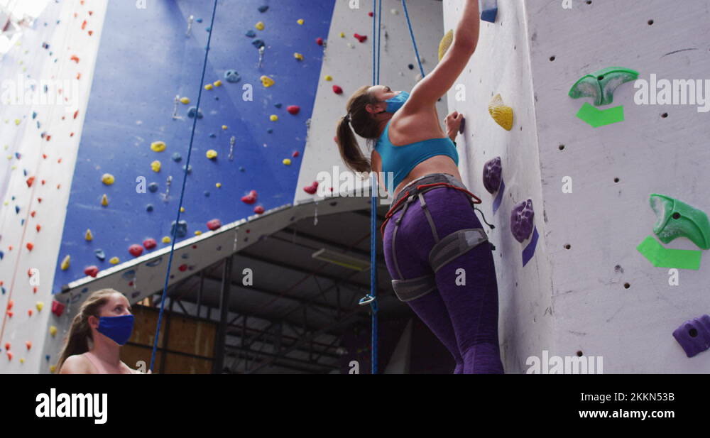 Two caucasian women wearing face masks using ropes to climb wall at ...