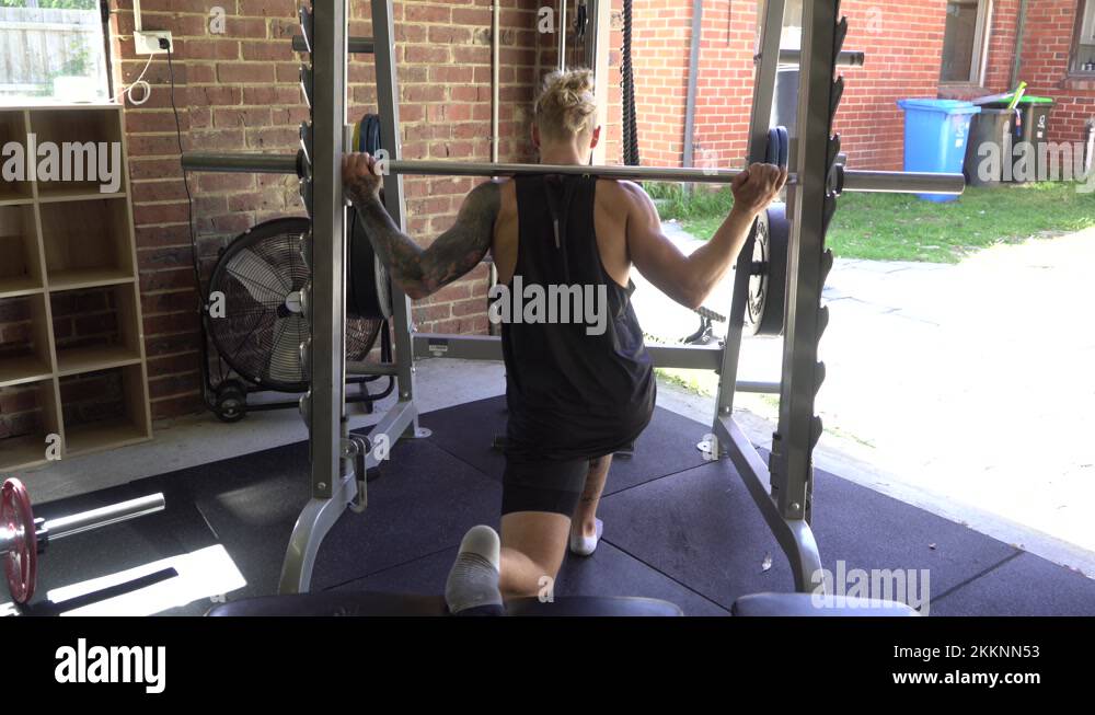 Tattoo man muscles in home gym back leg raise smith machine lunge Stock ...