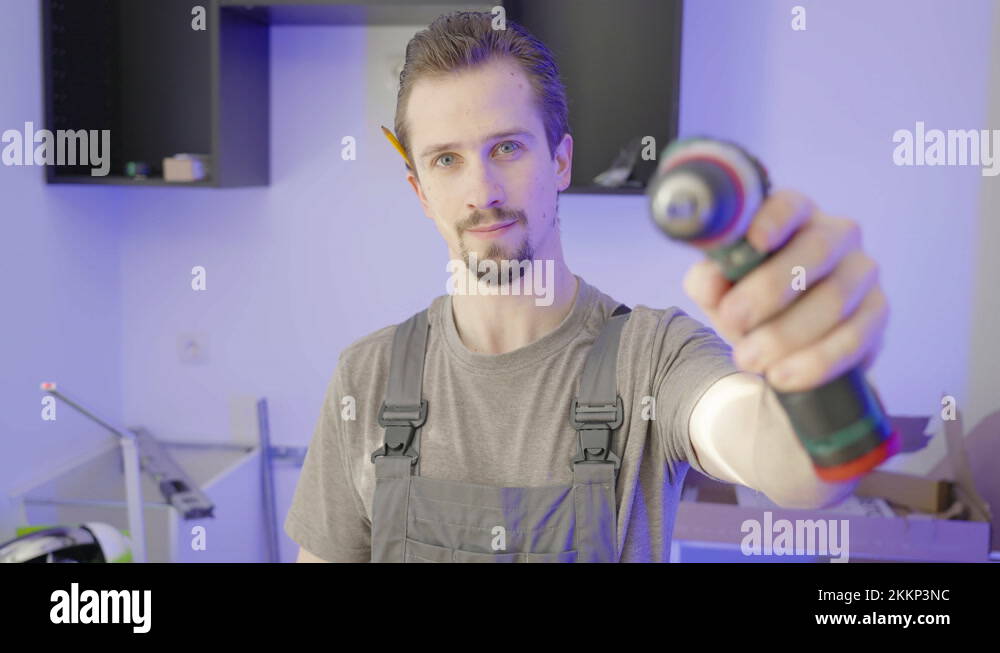 Kitchen carpenter shooting the camera with electric screwdriver and ...