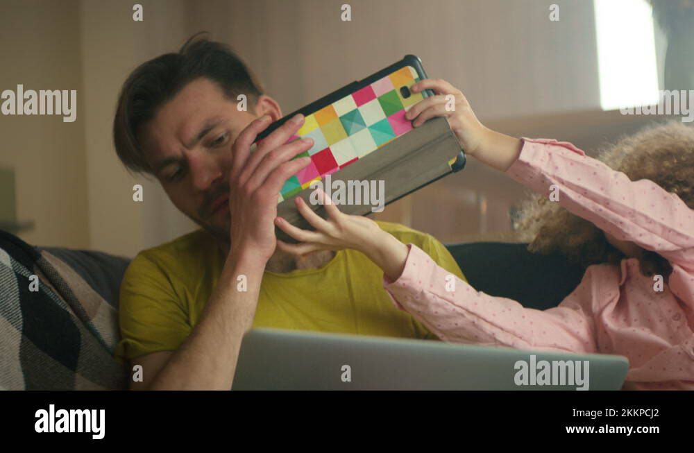 Young Dad Sitting On Sofa With Laptop. An Eight Year Old Girl Shows Him ...