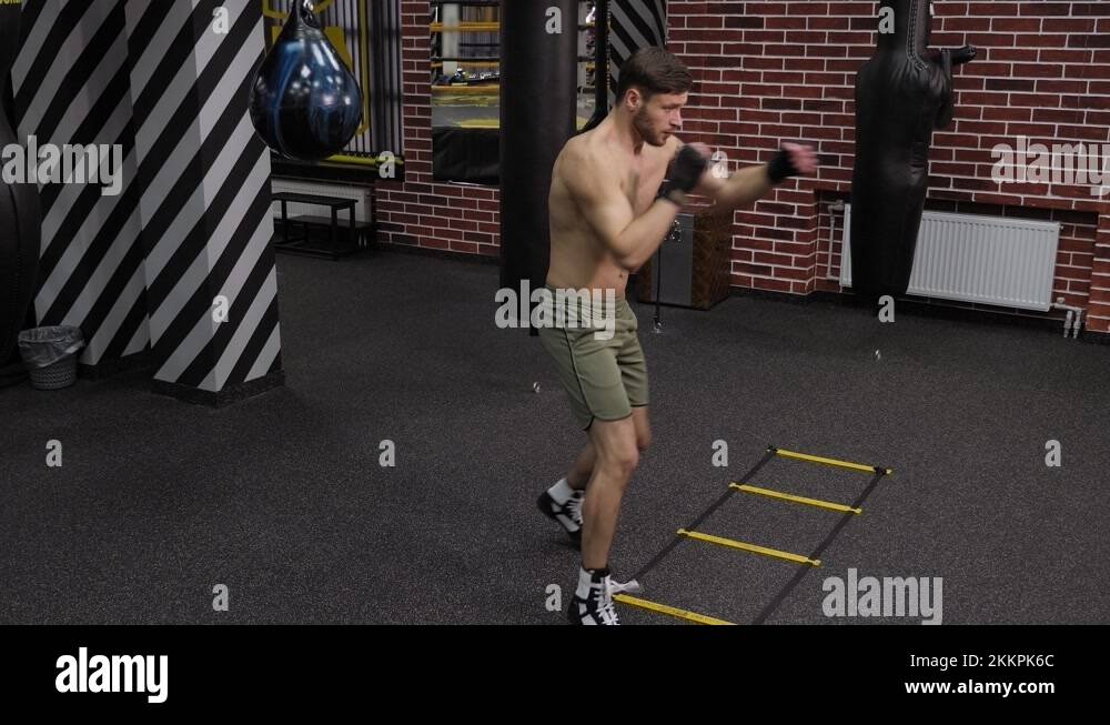 A muscular male boxer with a bare torso trains on a boxing ladder in ...