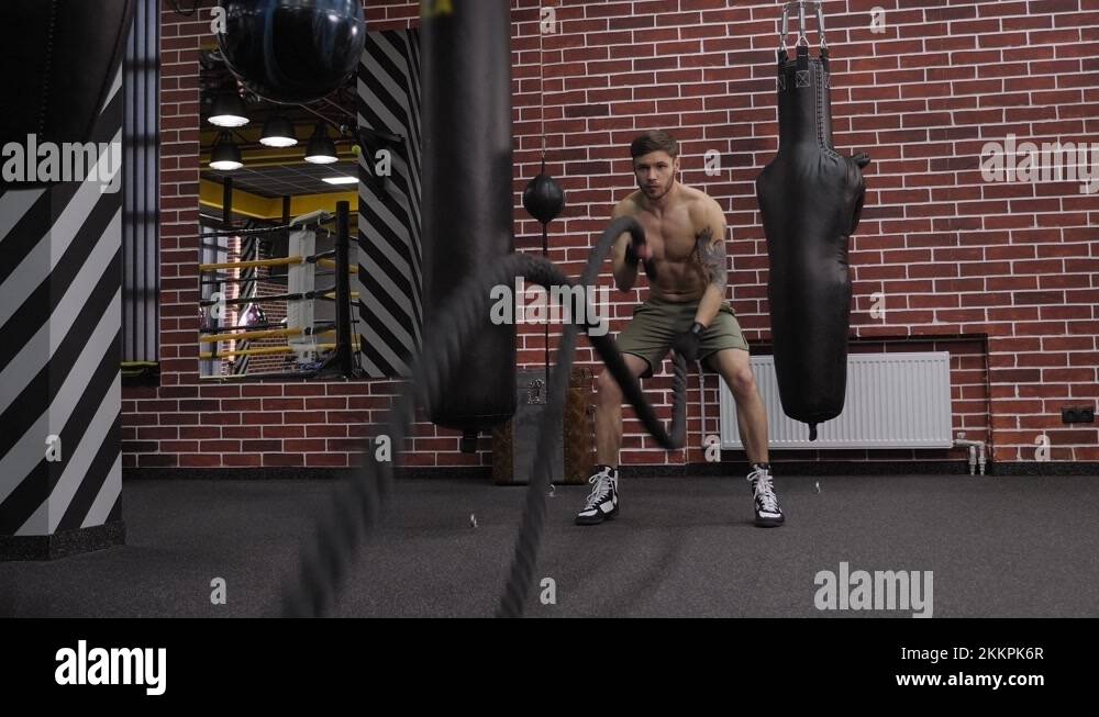 A muscular male boxer does an exercise with ropes in a sports gym Stock ...