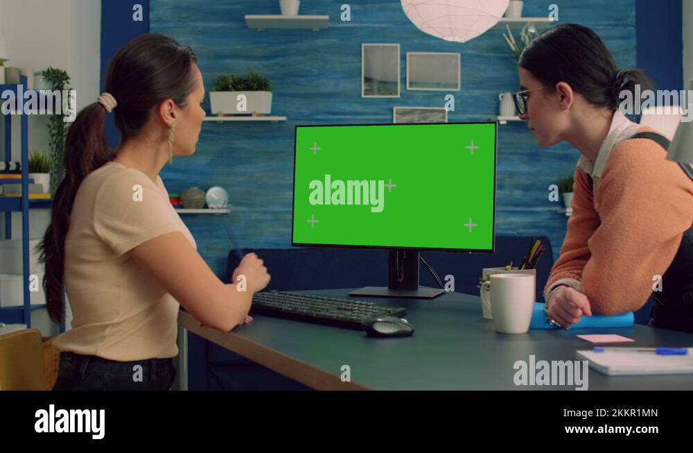 Two collegues working together on computer with mock up green screen ...