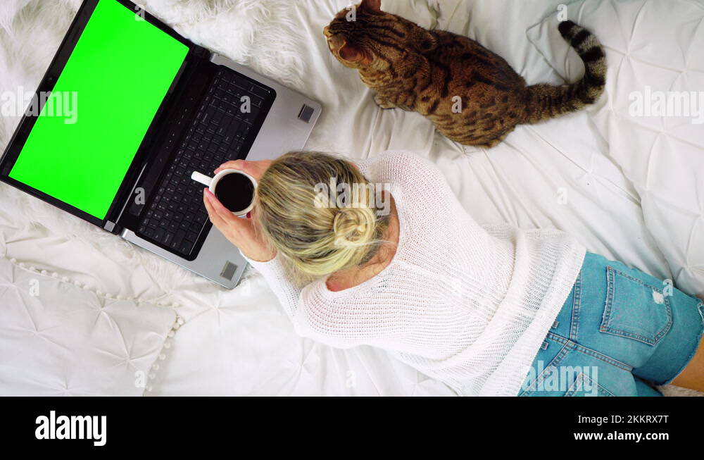 Top-down view of woman lying on bed looking at blank green screen of ...