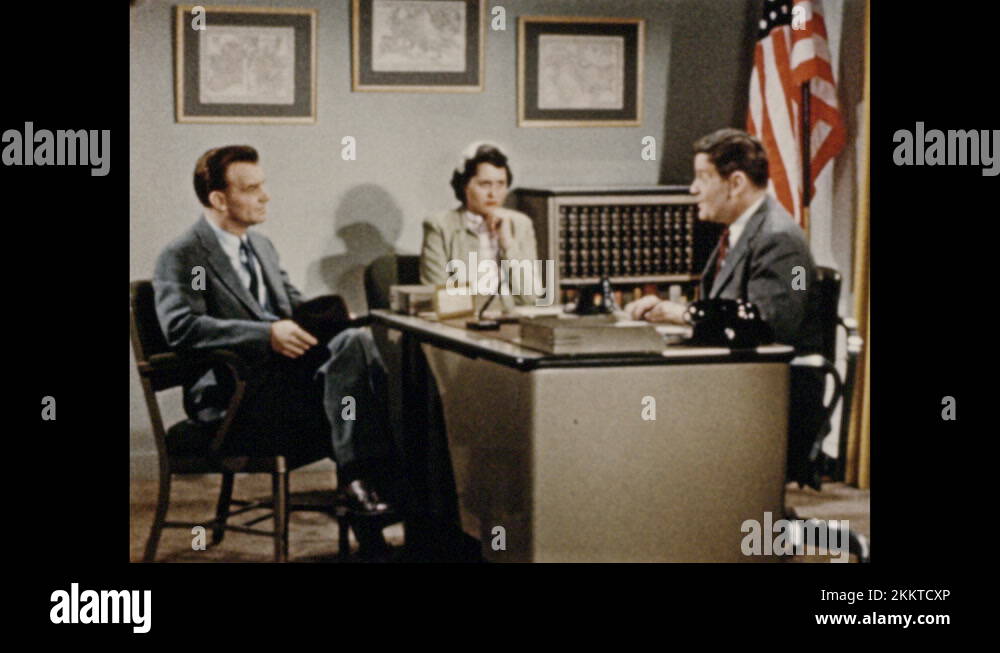 1950s: Man sits in front of desk in office listening to man behind desk ...