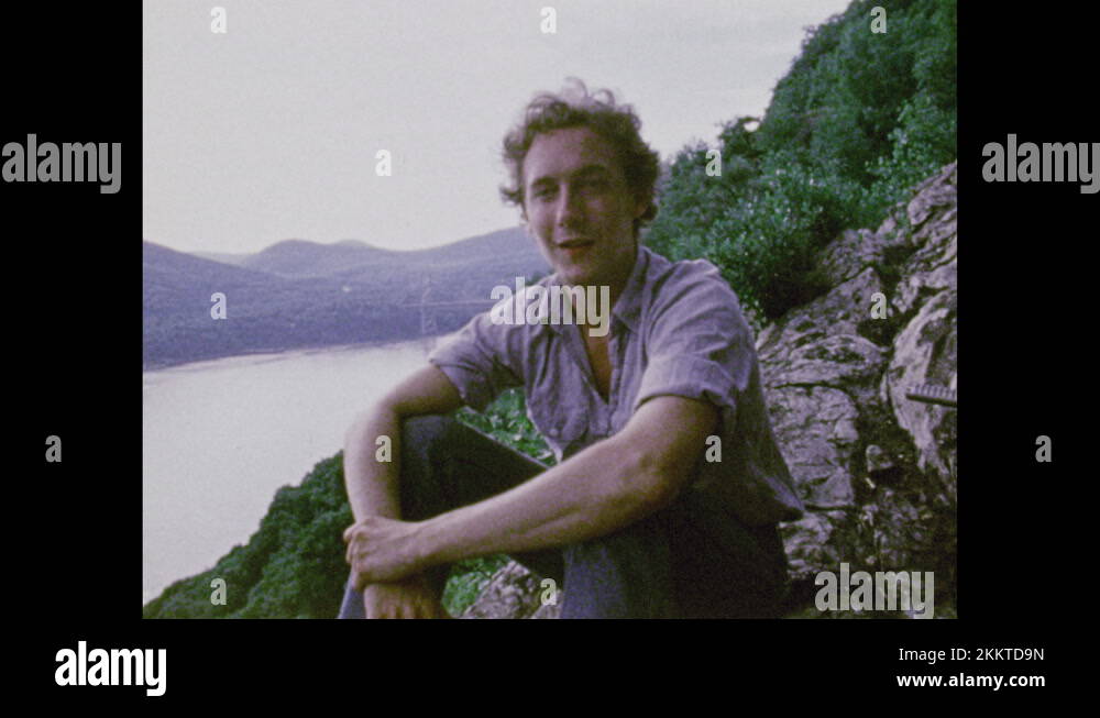 1970s: Teen boy sits next to lake on rock and talks. Film in reverse ...