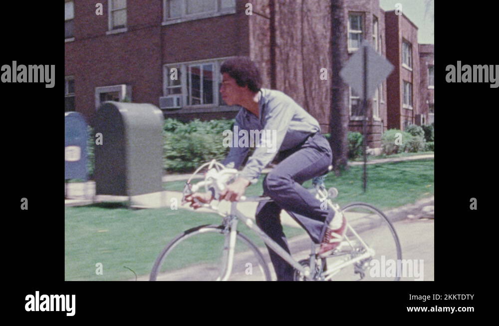 1970s: Feet pedaling. Tracking shot, boy on bike, raises arm, turns ...