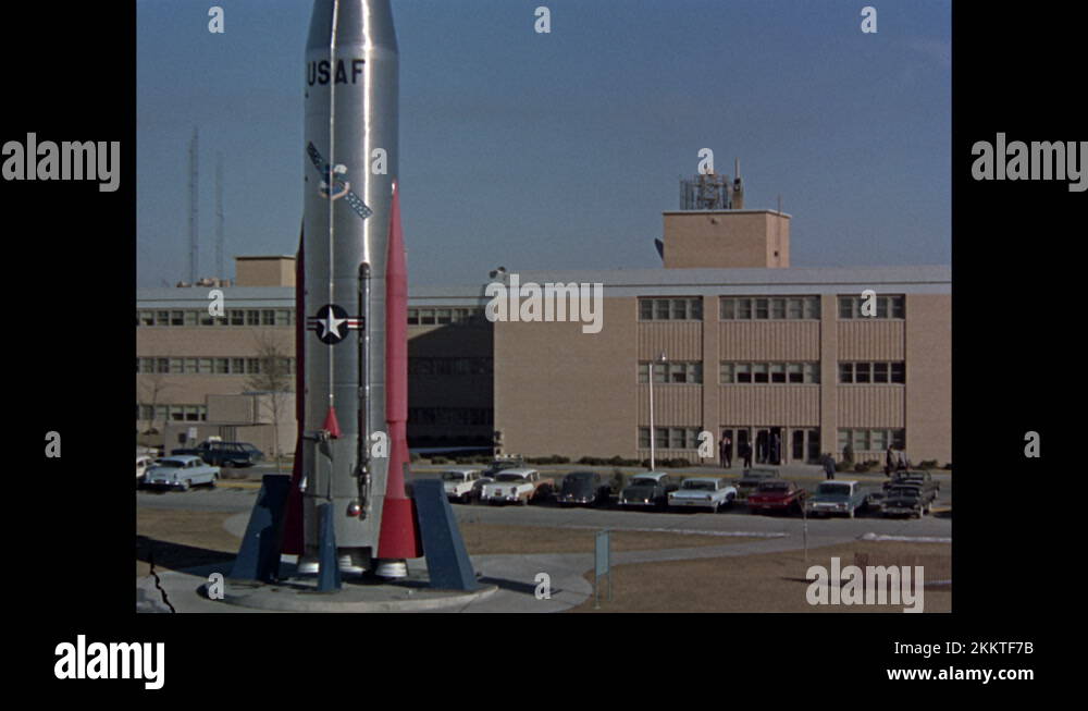 1960s: USAF rocket mounted outside of building and parking lot, people ...