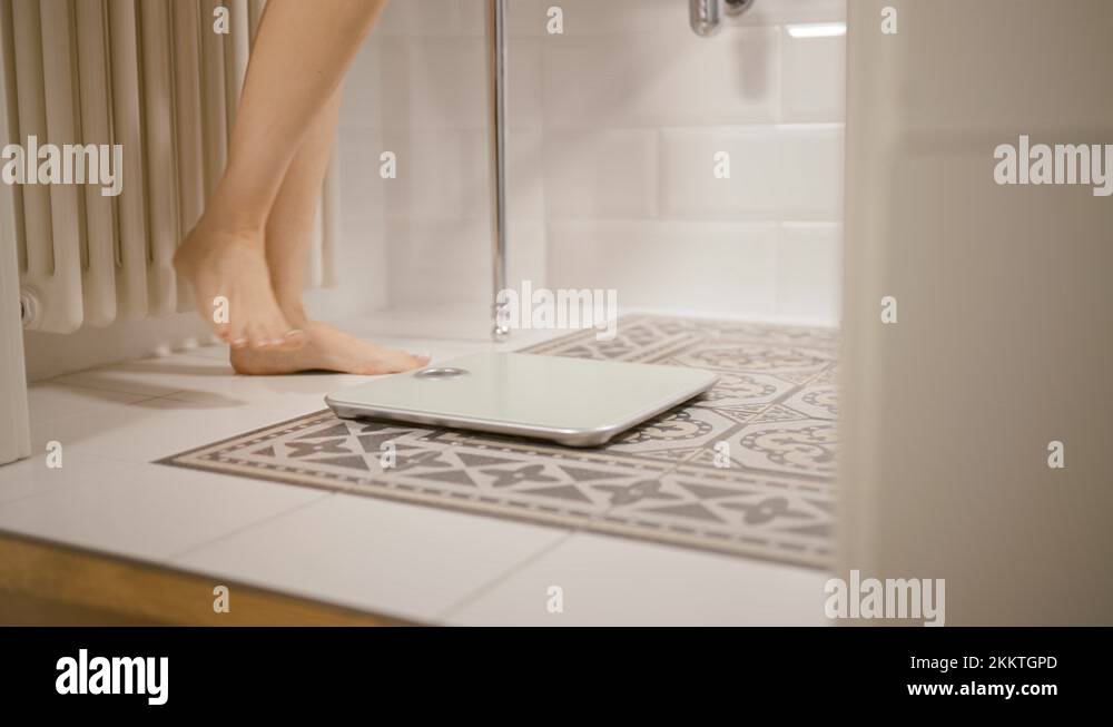 Legs of skinny woman with smooth skin standing on scales to check her ...