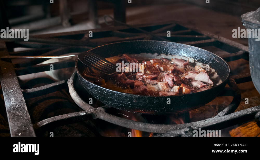 Frying meat in pan on the opened fire at fireplace in house inside ...