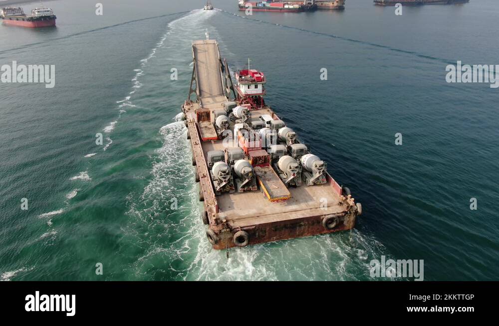 Barge loaded with Concrete mixer trucks pulled to port by a Tugboat in Stock Video Footage - Alamy