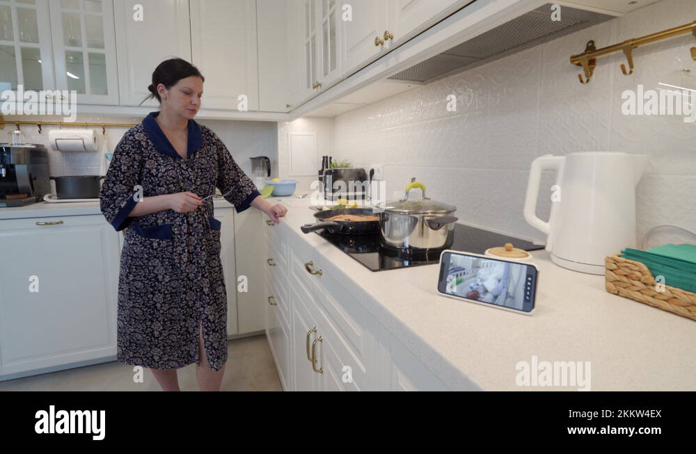 Mother cooking dinner in the kitchen using ip camera as baby video ...