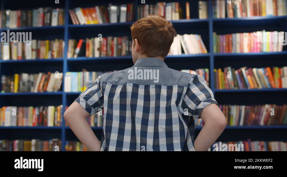 Back view of teen boy choosing book on bookshelf in library Stock Video ...
