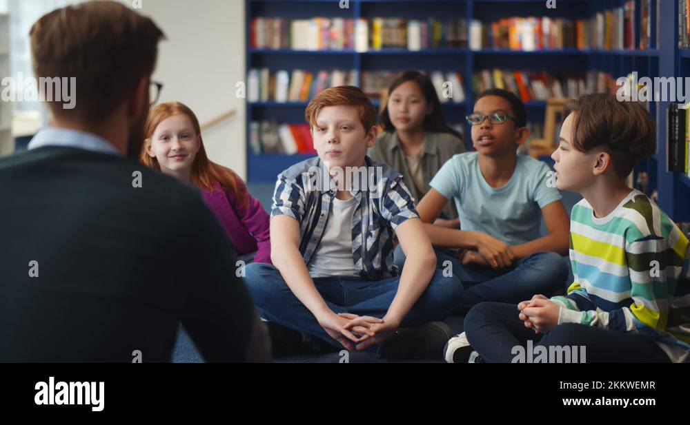 Back view of teacher with class visiting library discussing books for ...