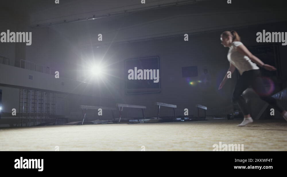 Girl gymnast performs somersaults forward in the gym on a gymnastic mat ...