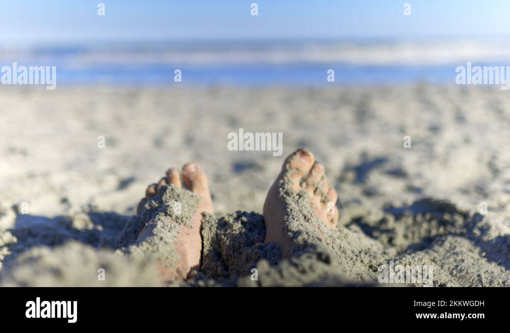 Adorable little girl kicking sand at adult feet on the beach Stock ...