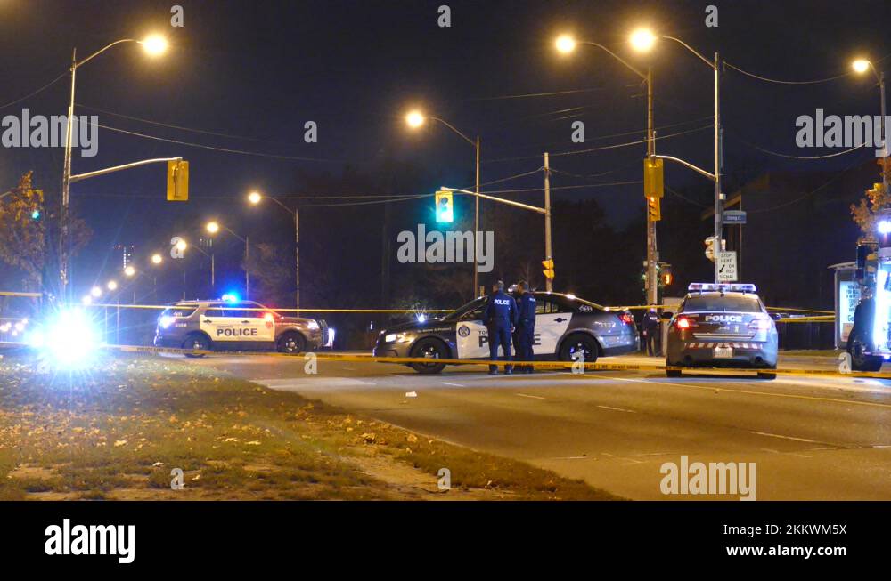 Cops near police cars with siren lights on, behind a caution yellow ...
