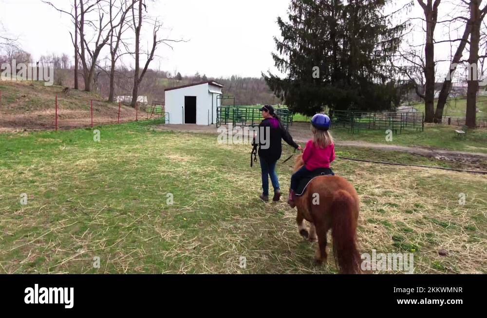 Young girl horseback riding and being led on miniature horse by woman ...