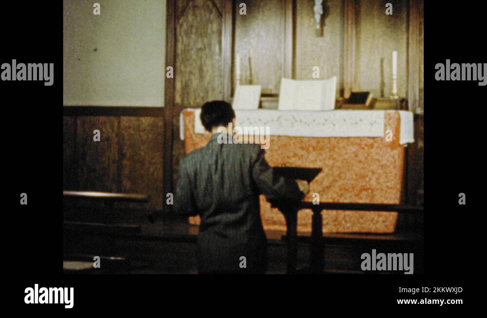 1950s: Church. Priest kneels and prays at altar. Sculpture of Jesus on ...