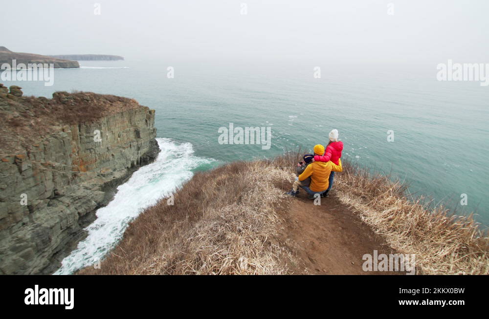 Father holds his kids on the cliff edge and shows them beautiful ocean ...