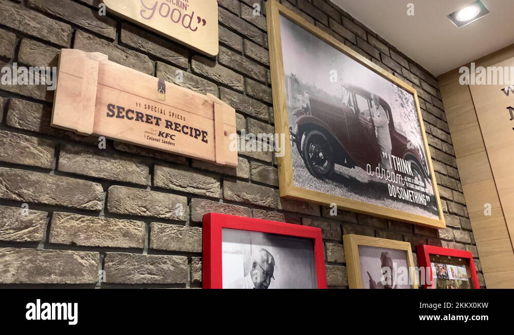 Framed photographs of the KFC owner on the wall. Grey brick wall with ...