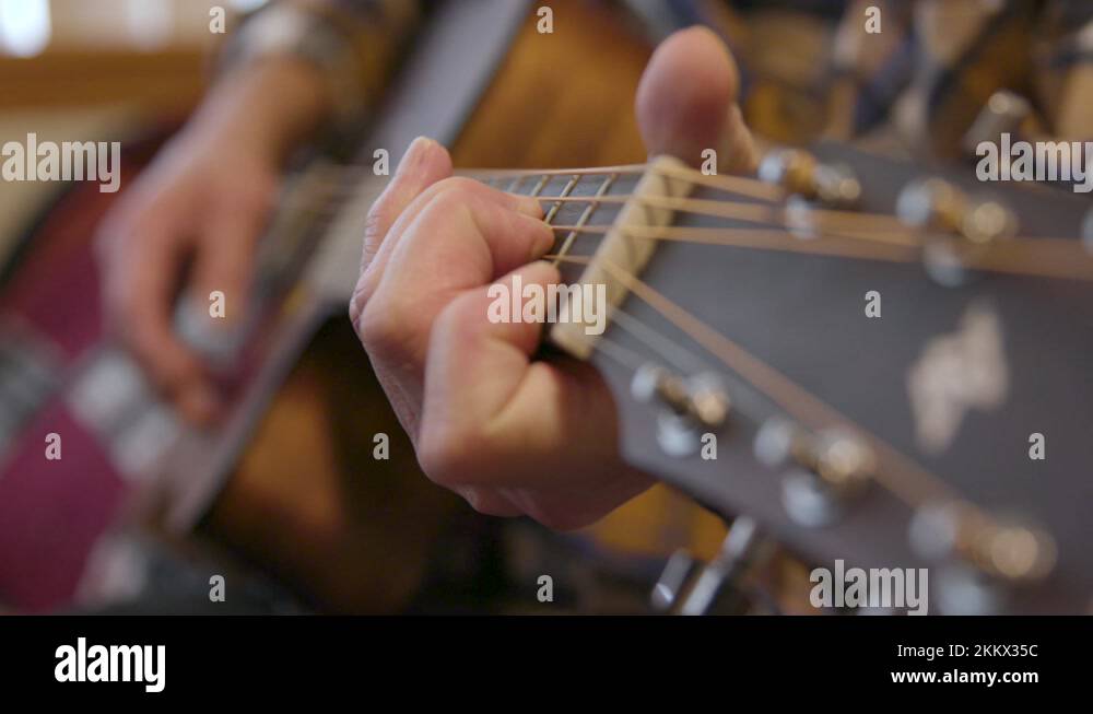 Focus shift shot of man's hand as he plays chords on his acoustic ...