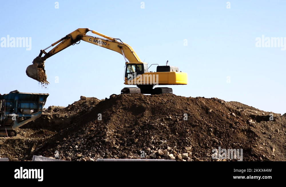 Digger dumping soil into a truck, vehicle positioned on mound of earth ...