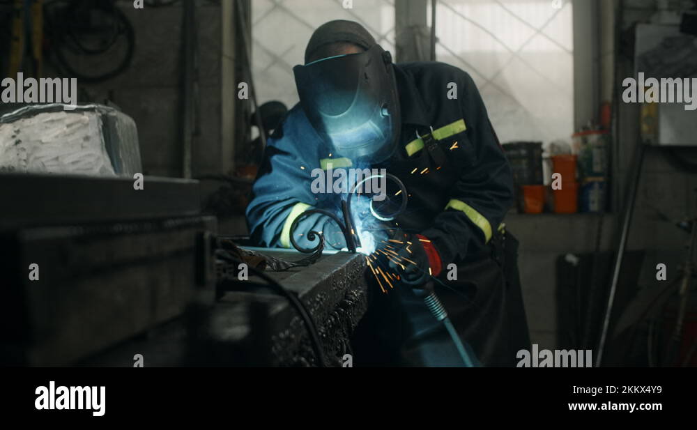 Welder welds metal details in safety uniform at his workroom, welding ...