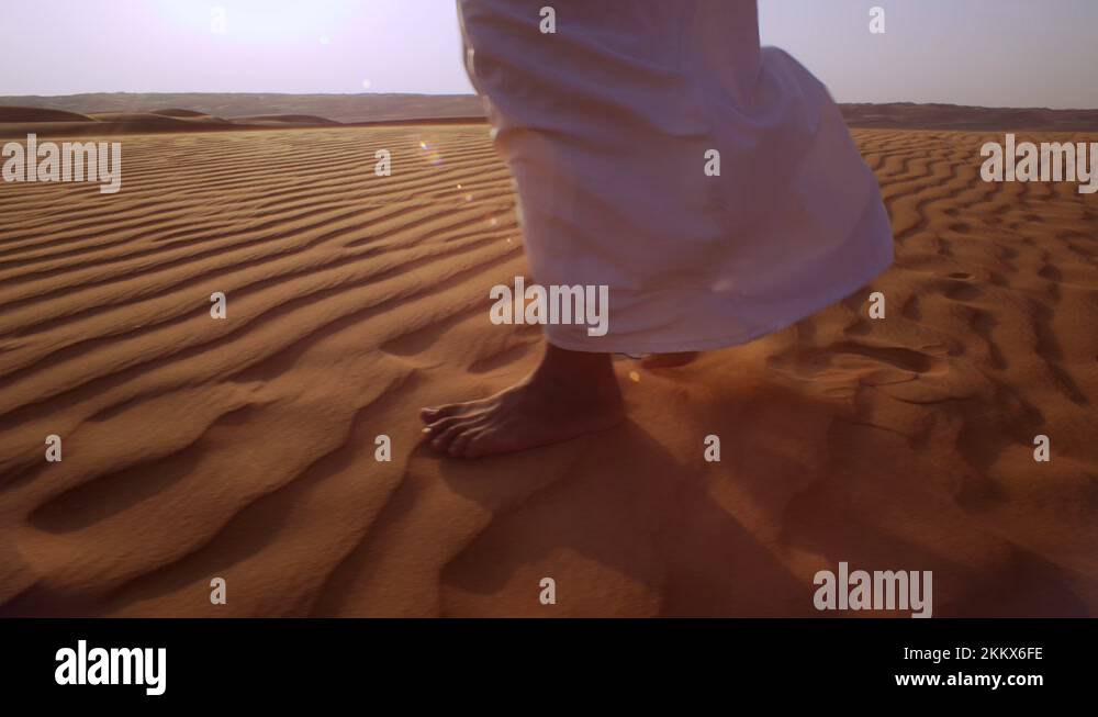 Omani Arab Man in national white tunic walking barefoot in desert sand ...