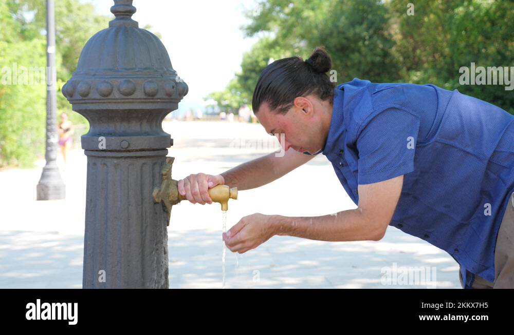 Man stand stooping against street fountain, flatten hair by hand and ...