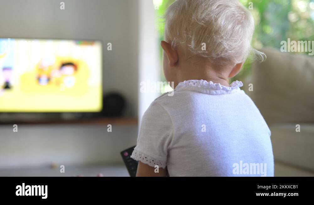 Back view of little baby girl sitting on the floor watching the ...