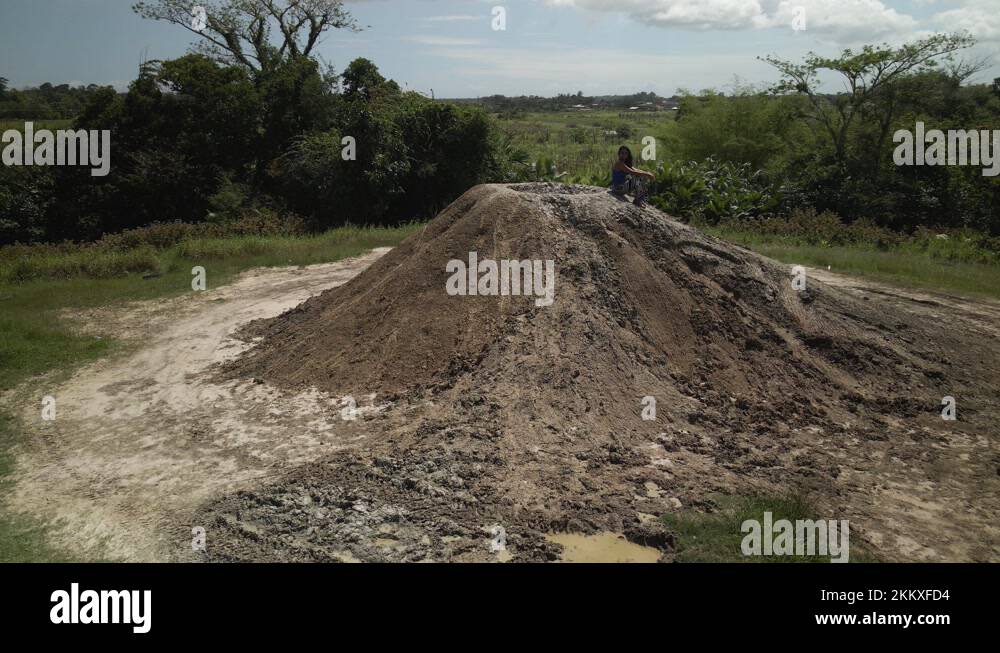 Aerial 360 pan of a girl sitting on a cone shaped mud volcano on the ...