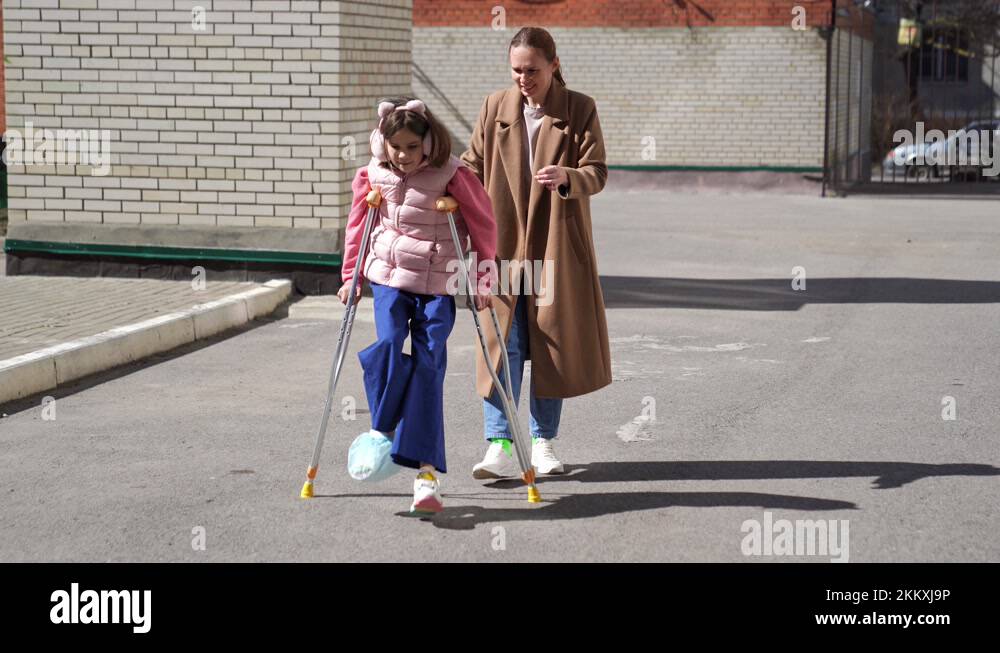 Mom Helps Her Daughter Learn To Walk On Crutches Plaster On Your Feet