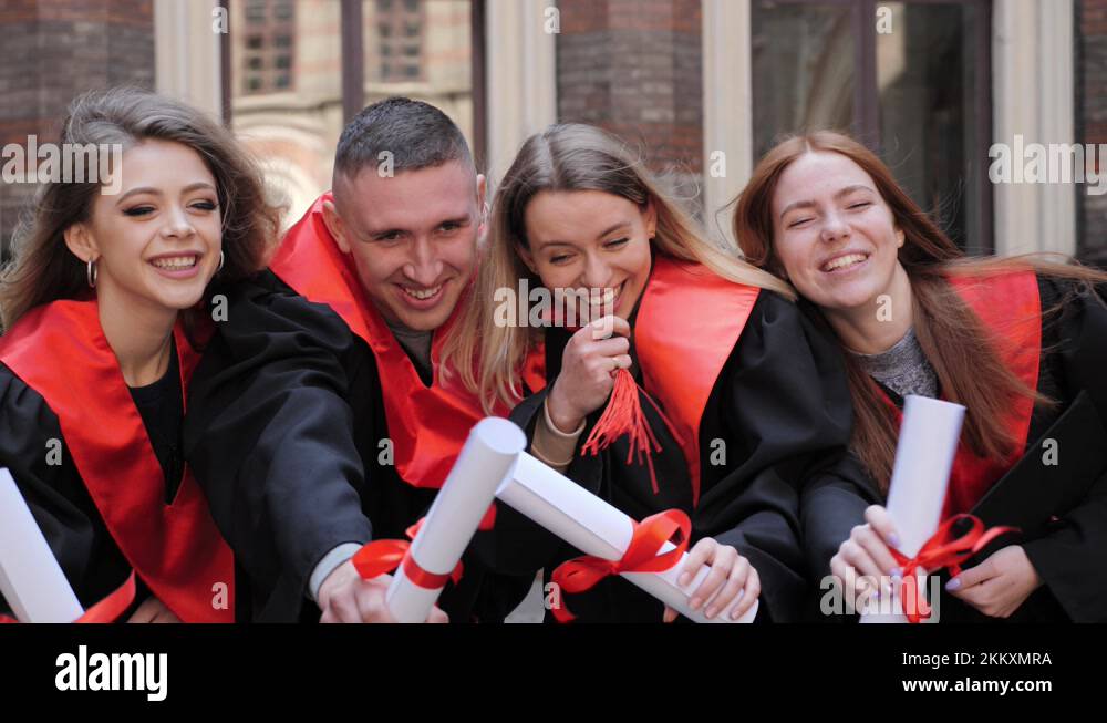 Students graduates in academic gowns with diplomas in hand posing for ...
