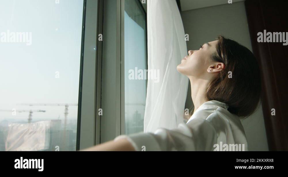 Young girl opening curtains on window in morning. Woman ready to start ...