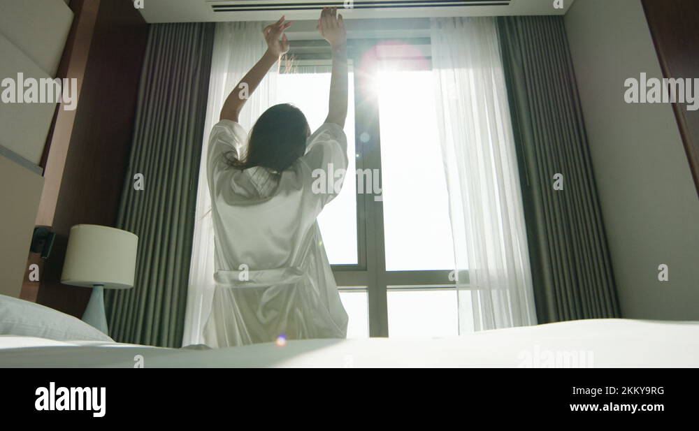 Girl waking up in cozy room in morning, stretching her arms and back ...