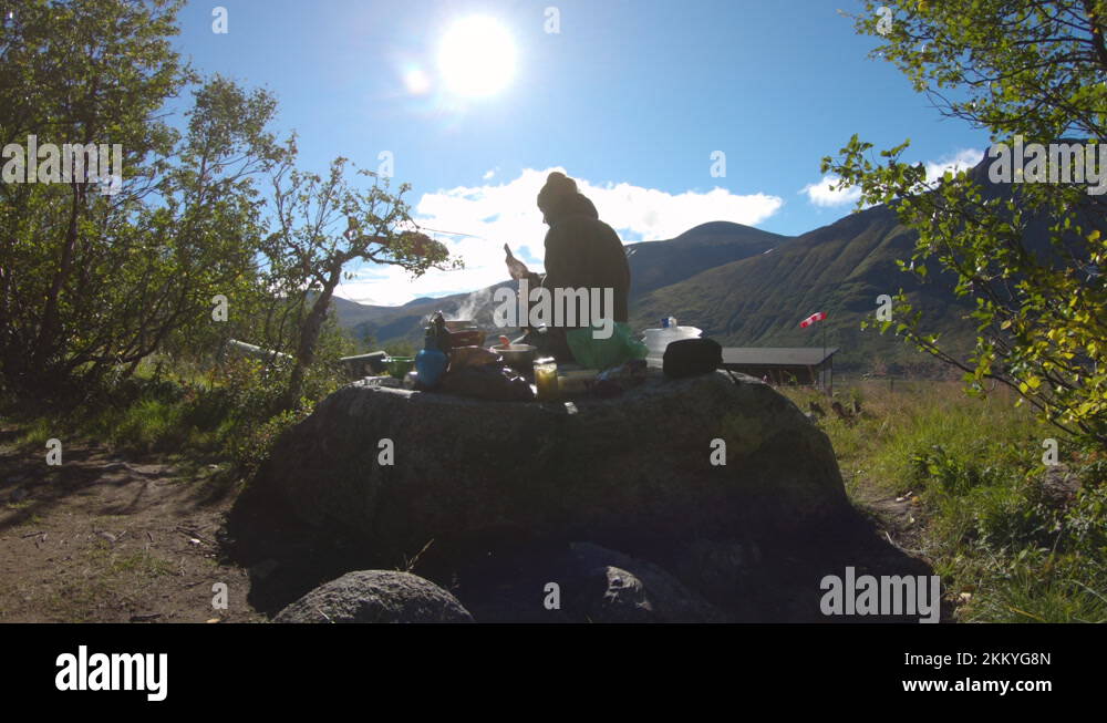 Female hiker eating breakfast on a big rock in the nature. You can see ...