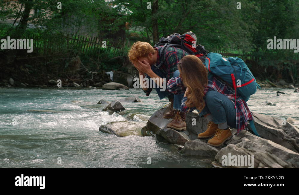 Couple of tourists having rest at river. Guy washing face with water ...