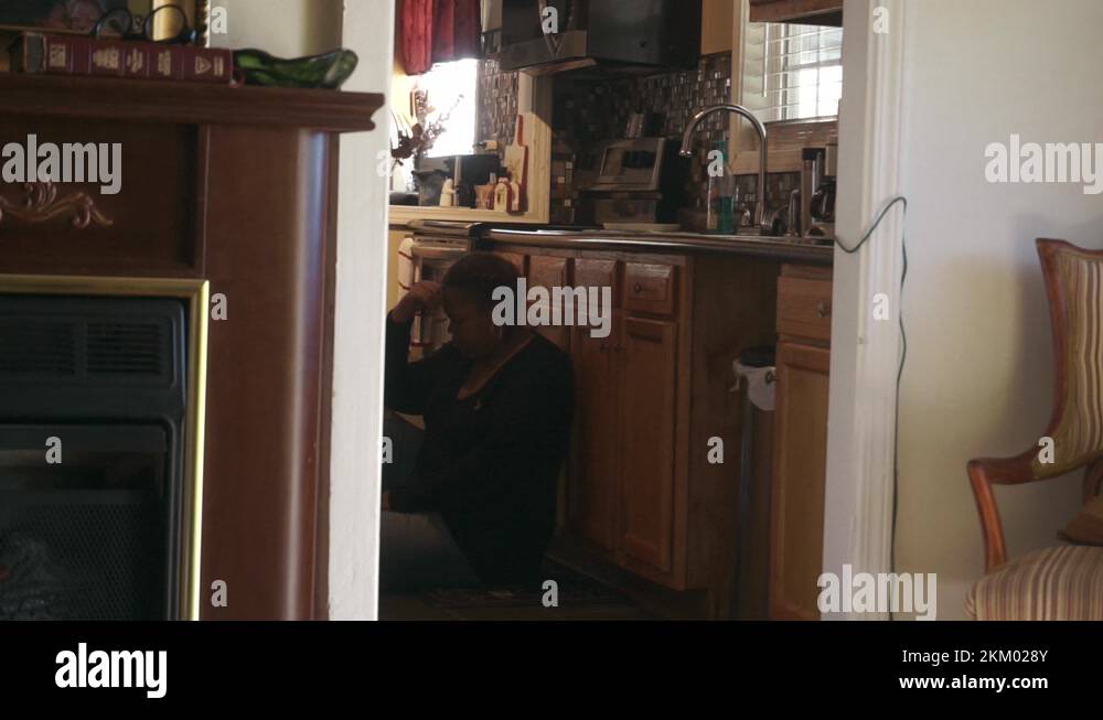 Slow zoom in of Sad black woman sitting on kitchen floor crying from ...