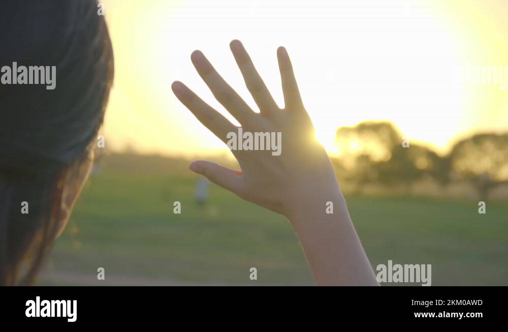 A girl shielding her eyes from sunlight to see field scenery at sunset ...