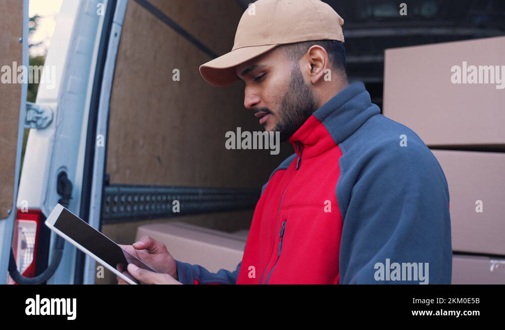 Young indian man using tablet to check delivery order. Loading truck ...