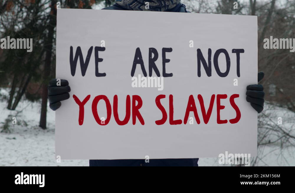 Person is standing and holding a White Sign that says We Are Not Your ...