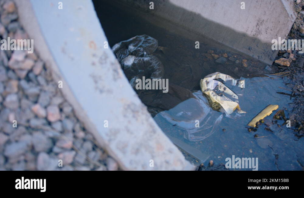 Slow pan from above of trash in shallow water by sewage system outdoor ...
