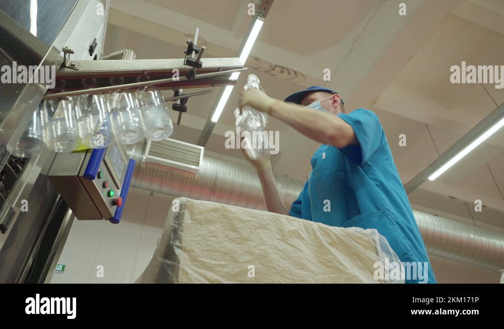 Operator takes plastic bottles from a container and loads them into a ...