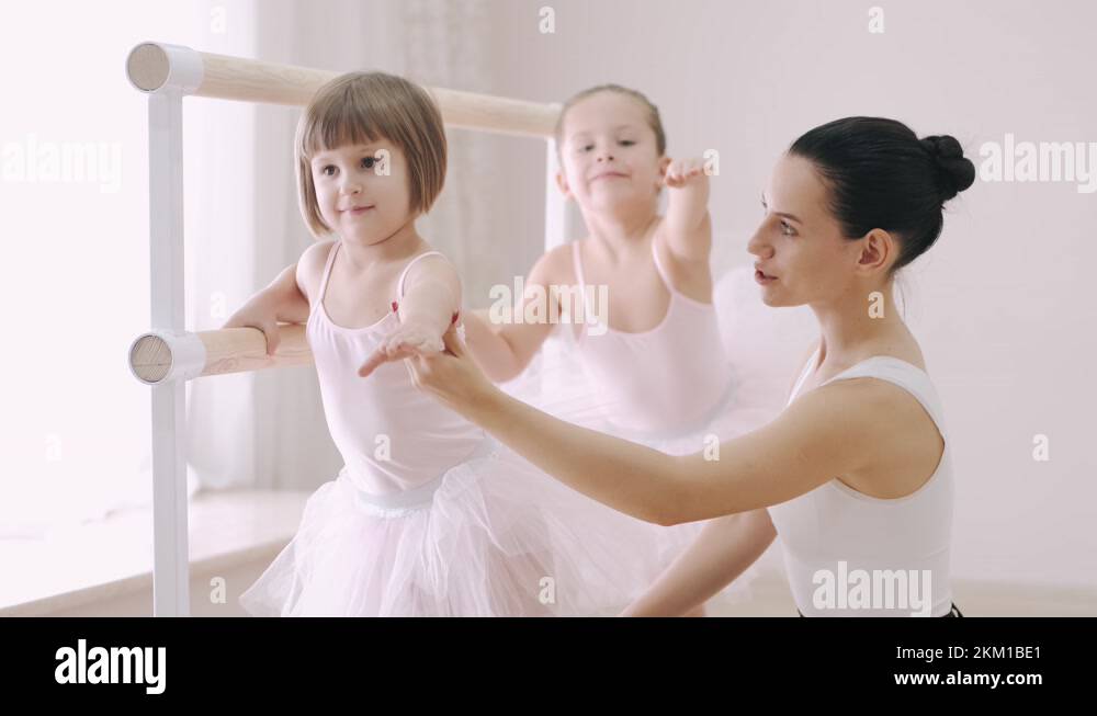 Two little girls practicing choreographic elements on ballet barre with ...