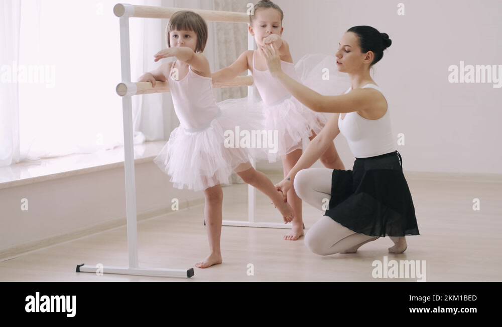 Two little girls practicing choreographic elements on ballet barre with ...